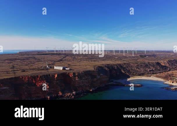 Wind turbines line the hillside overlooking the ocean. A small building ...