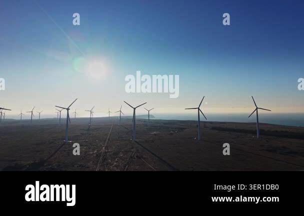 Wind turbines are visible on a hill with open land and the sea in the ...