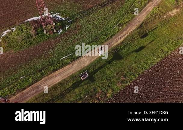 Two vehicles are parked on a dirt road in a field. A power line tower ...