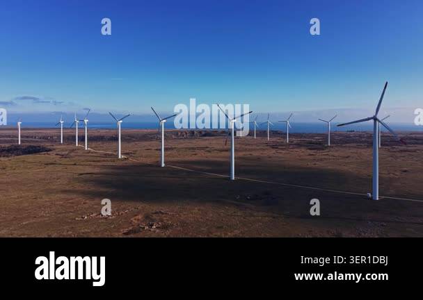 Wind turbines are lined up on a flat area near the coast. The sky is ...