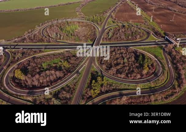 Cars are traveling along a large road intersection surrounded by green ...
