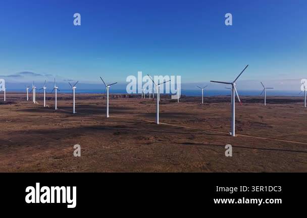 Wind turbines are lined up in a vast area near the ocean. The clear ...
