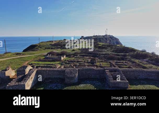 Visitors explore ancient ruins located on a coastal area. The sun ...