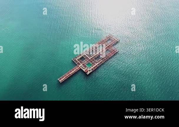 A mussel farming platform sits in clear blue water. Workers are ...