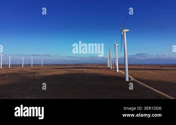 Wind turbines are aligned in a row on flat land. The sky is clear and ...