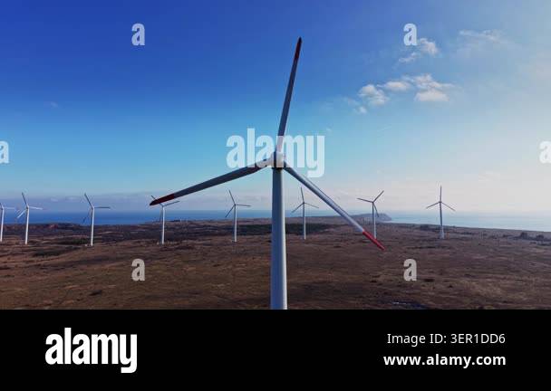 Wind turbines are located on land near the coast. They spin as the wind ...