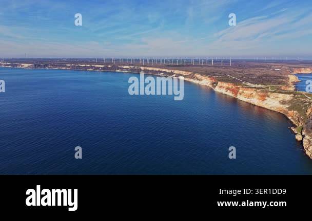 Cliffs rise above the water at the coast. Wind turbines can be seen in ...