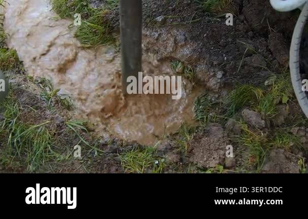 Workers are drilling a water well in a grassy field. Water is flowing ...