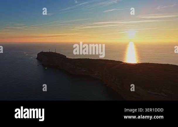 The sun sets over a rocky coastline as light shines on the water. Wind ...
