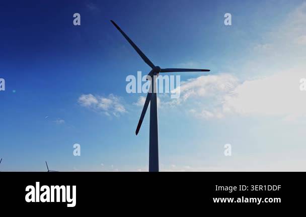 A wind turbine stands tall against the blue sky. The blades rotate ...