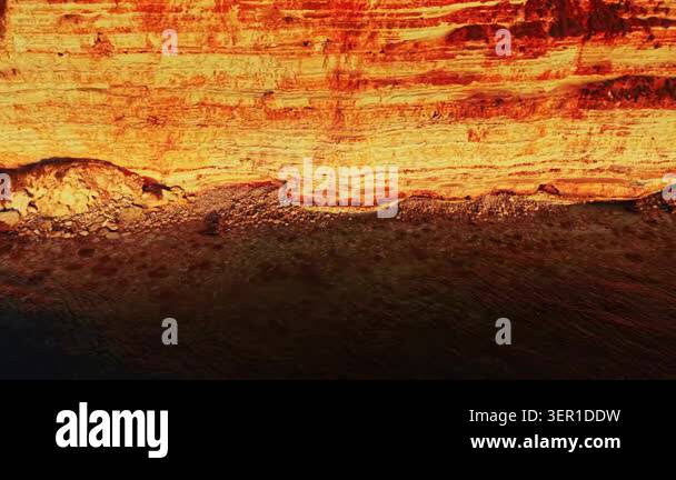 The scene shows a cliffside with layers of color along the shore. The ...