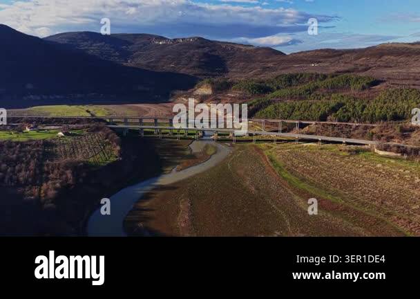 A bridge stretches across a river surrounded by fields and hills. The ...