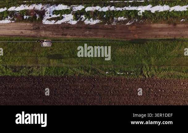 A cable car moves above green fields and dirt paths. Snow patches are ...