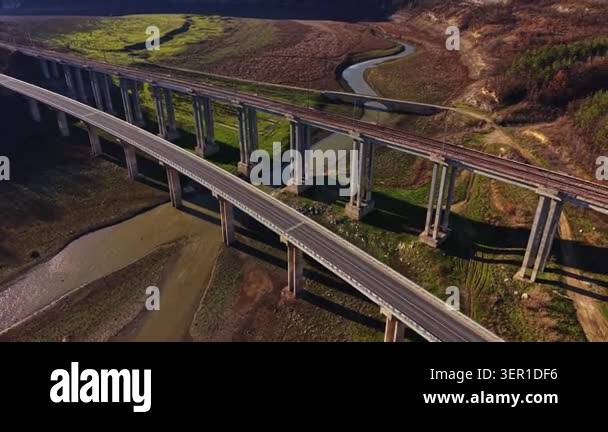 Train tracks rise above a river in a rural area. The landscape shows a ...