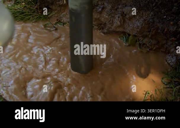 Workers are drilling into the ground to reach water. Muddy water flows ...