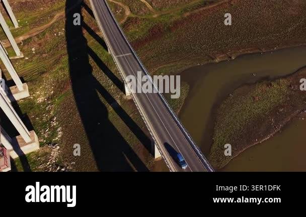 A car travels along a road beneath a tall bridge. The sunlight creates ...
