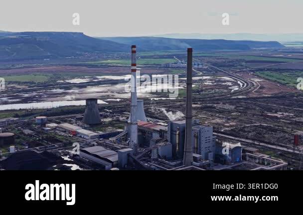 Workers and vehicles are present at an industrial area with smokestacks ...