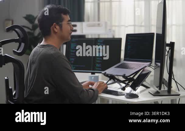 An individual is working intently at a desk with multiple screens ...