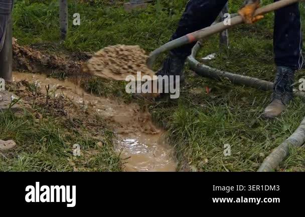 Workers use a shovel to dig a trench for a water well. The ground is ...