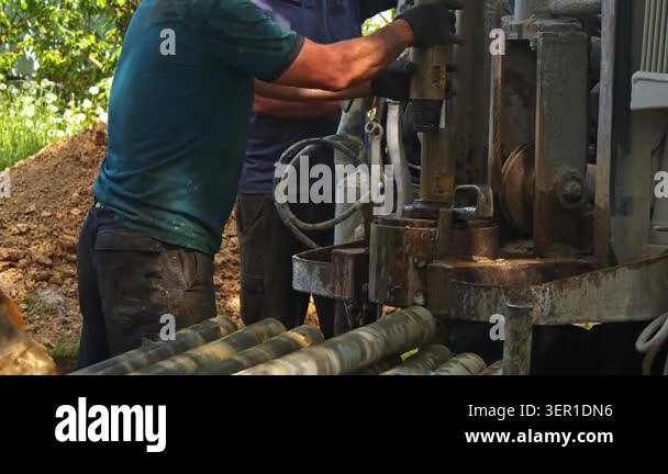 Two workers operate a drilling machine to create a water well in a ...