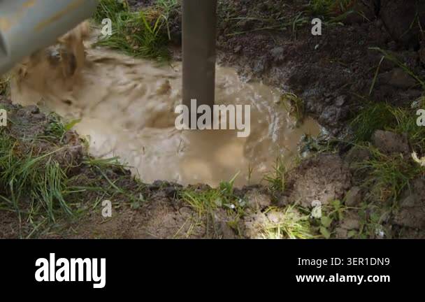 Workers are drilling a water well in a rural area. Water flows out from ...