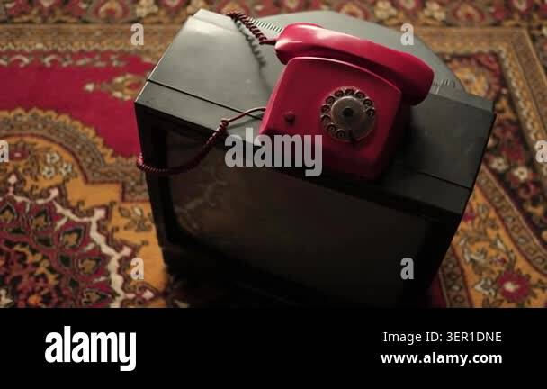 A red rotary telephone rests on an old black television against a ...