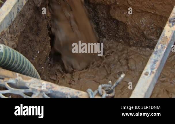 Workers drill a water well deep into the ground, causing mud and debris ...