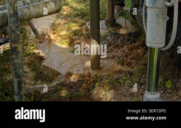 Workers are drilling a water well in a grassy area. Water flows from ...