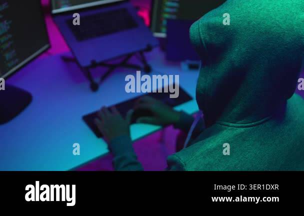 A hacker in a hoodie is intensely coding on a keyboard while surrounded ...