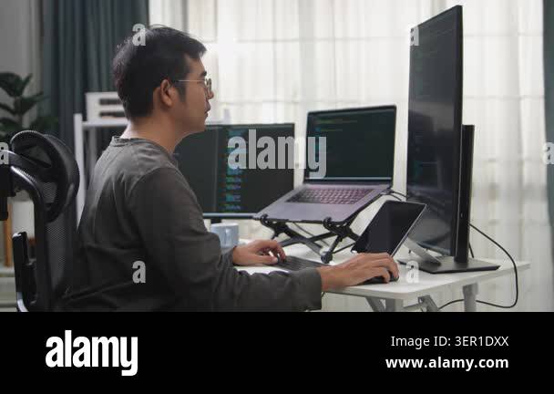 A programmer is engaged in coding on multiple computer screens in a ...