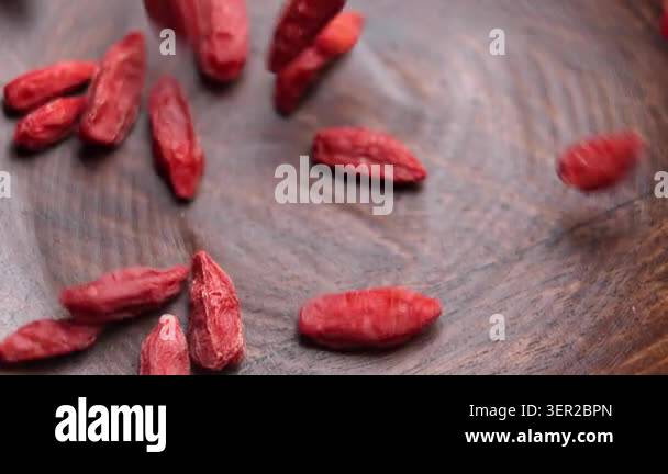 Dried goji berries falling into a rustic wooden bowl in slow motion ...