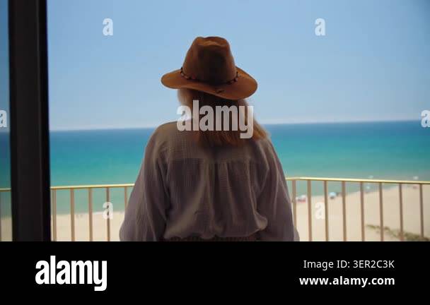 Woman walking from hotel room to balcony with panoramic sea view during ...