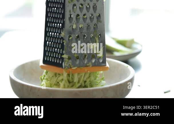 Close-up of a woman's hands grating a fresh green zucchini on a metal ...