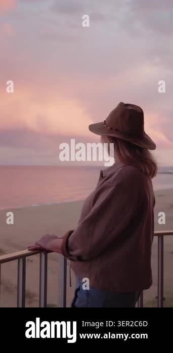 Woman in wide brim hat enjoying peaceful ocean view from balcony at ...
