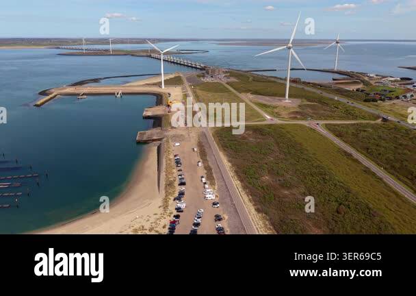 Aerial view of a coastal dam with wind turbines, a sandy beach, parked ...