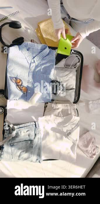Overhead shot of a woman packing a suitcase with summer clothes and ...