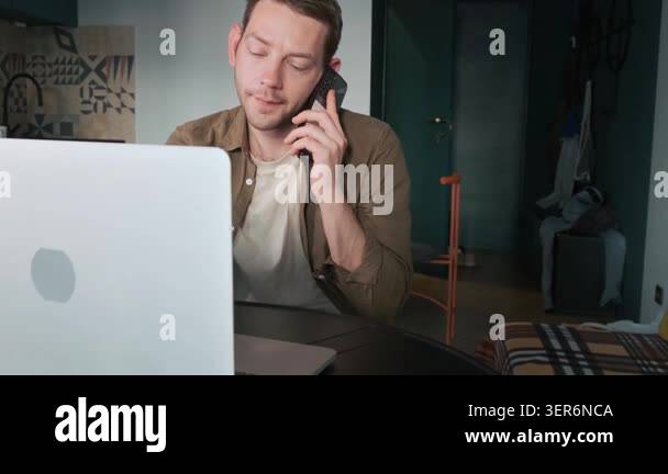 Man talking on smartphone while working on laptop at home office. Male ...