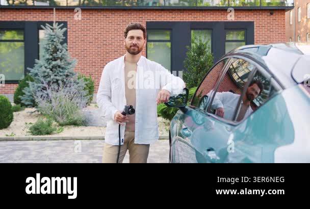 Handsome bearded man in a white shirt charging an electric car and ...