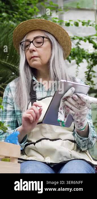 Confident appealing senior female gardener in glasses wearing straw hat ...