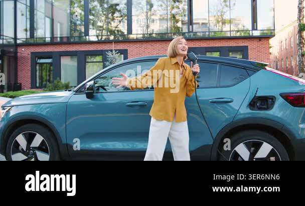 Cheerful young woman dances playfully while holding a charging cable ...
