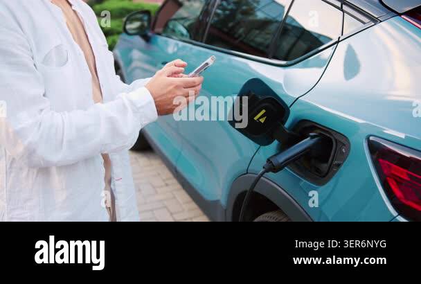 Man standing in front of an electric car, using a mobile app on a ...