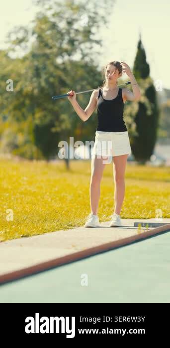 A woman practices her putting skills on a green surface. It is a sunny ...
