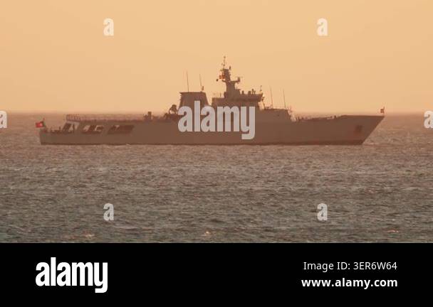 A warship is seen sailing on the ocean as the sun sets in the ...