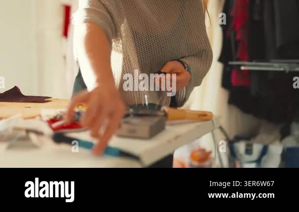 A designer works in a fashion studio, handling fabrics and tools. She ...
