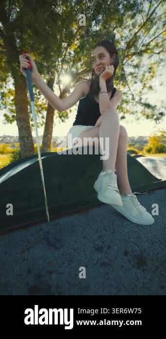 A young woman sits comfortably on the roof of a parked car. She relaxes ...