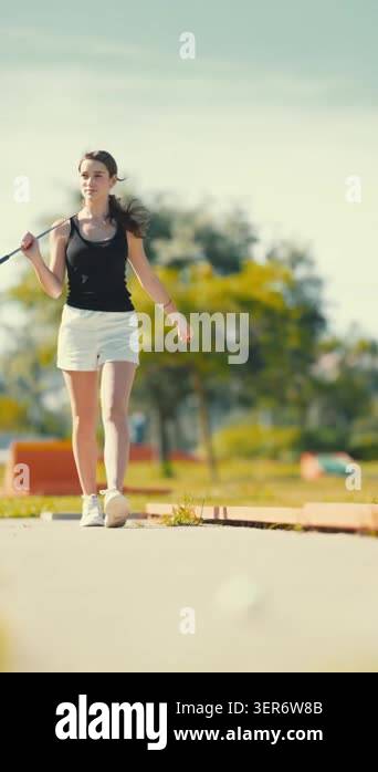 A woman walks along a path in a park while holding a golf club. She ...