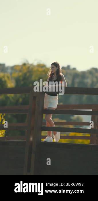 A woman stands on a wooden bridge in a park. She looks out over the ...