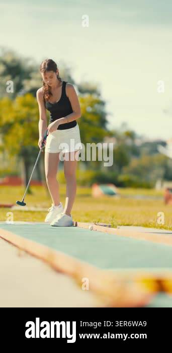 A woman makes practice strokes on a putting green at a golf course. She ...