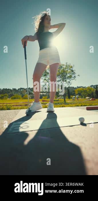 A golfer stands on the range practicing her swing. The sun shines ...