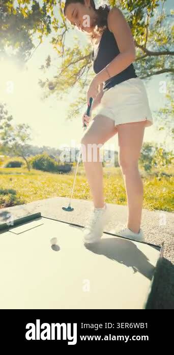 A girl stands near a mini golf course aiming to putt a ball. She shows ...
